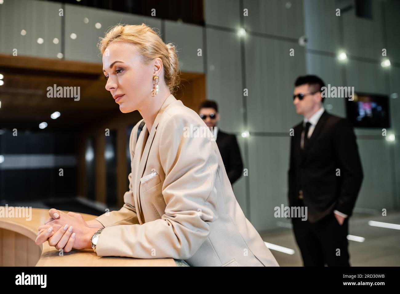 successful blonde woman in formal wear standing at reception desk ...