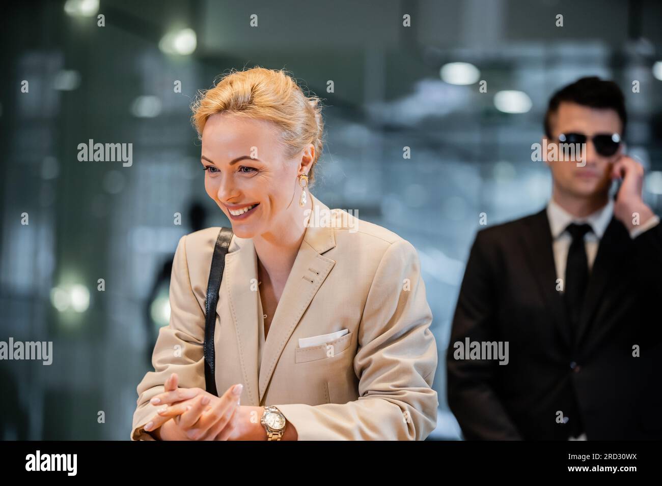 happy blonde woman in formal wear standing at reception desk, personal ...