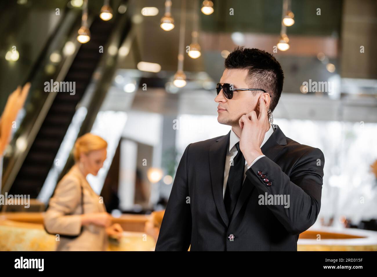 bodyguard in sunglasses, handsome man in suit and tie touching earpiece ...