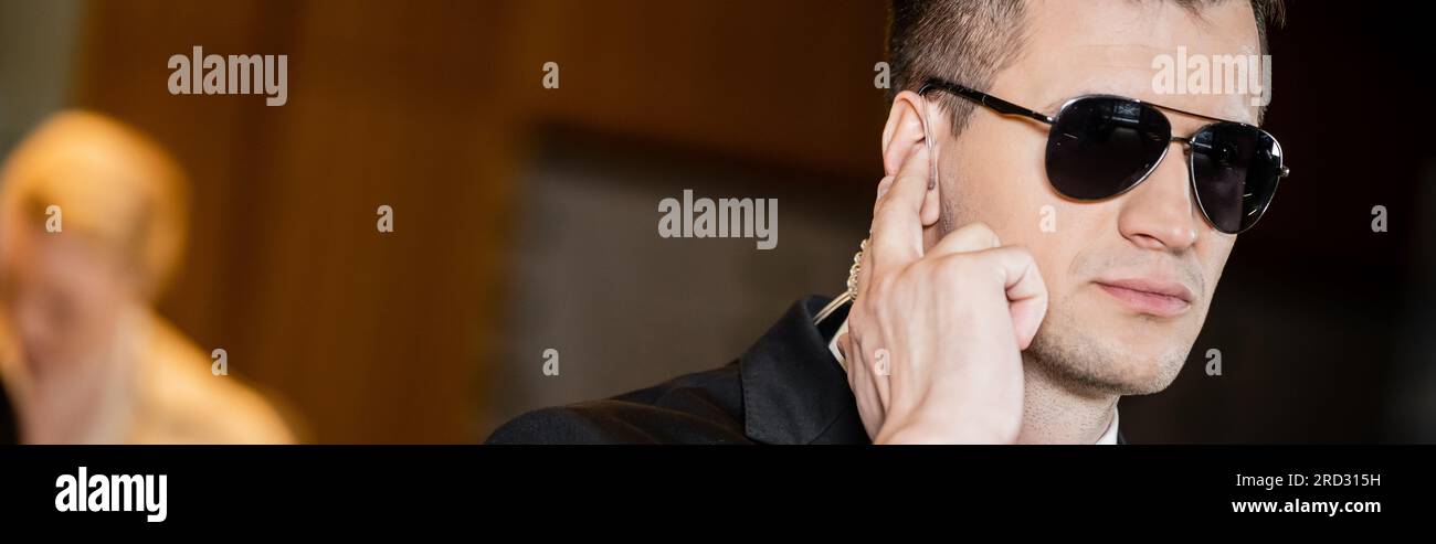 handsome bodyguard in sunglasses, man in suit and tie touching earpiece ...
