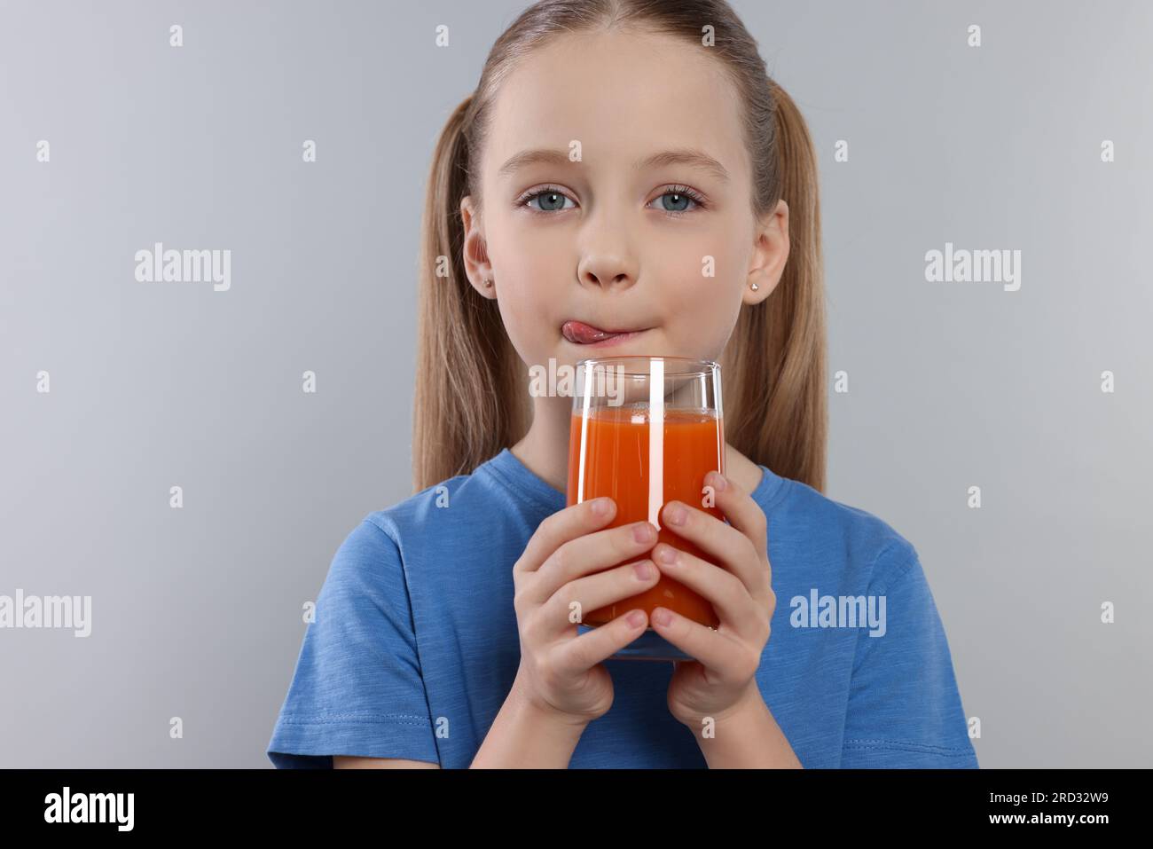 Cute little girl enjoying fresh juice on light gray background Stock ...