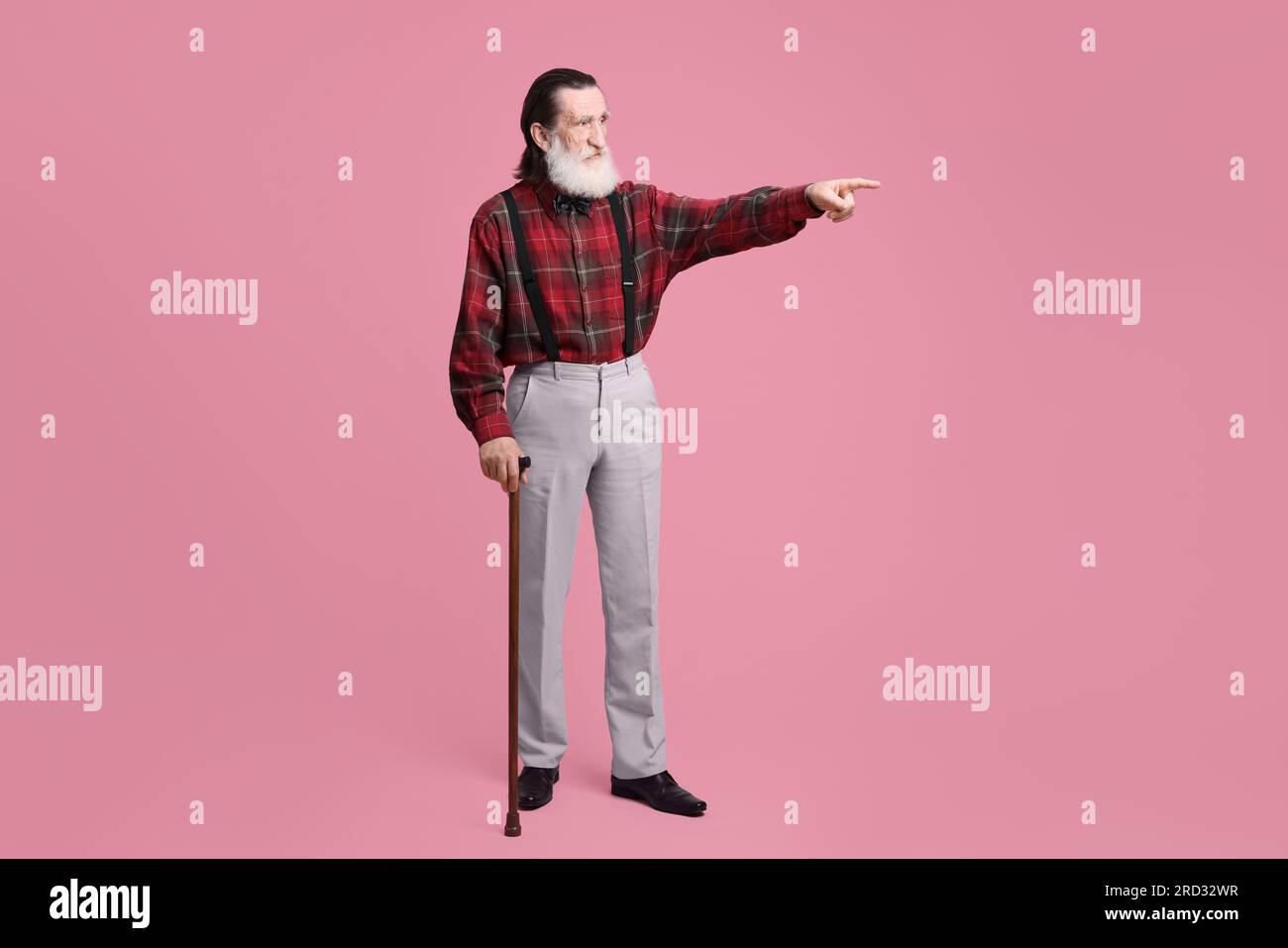 Senior man with walking cane pointing at something on pink background ...