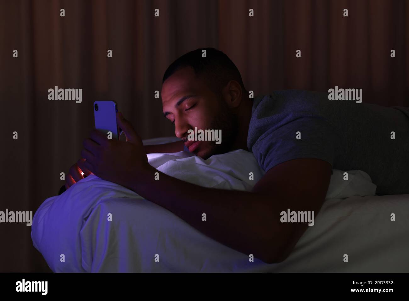 Young man sleeping while holding smartphone in bed at night. Internet ...