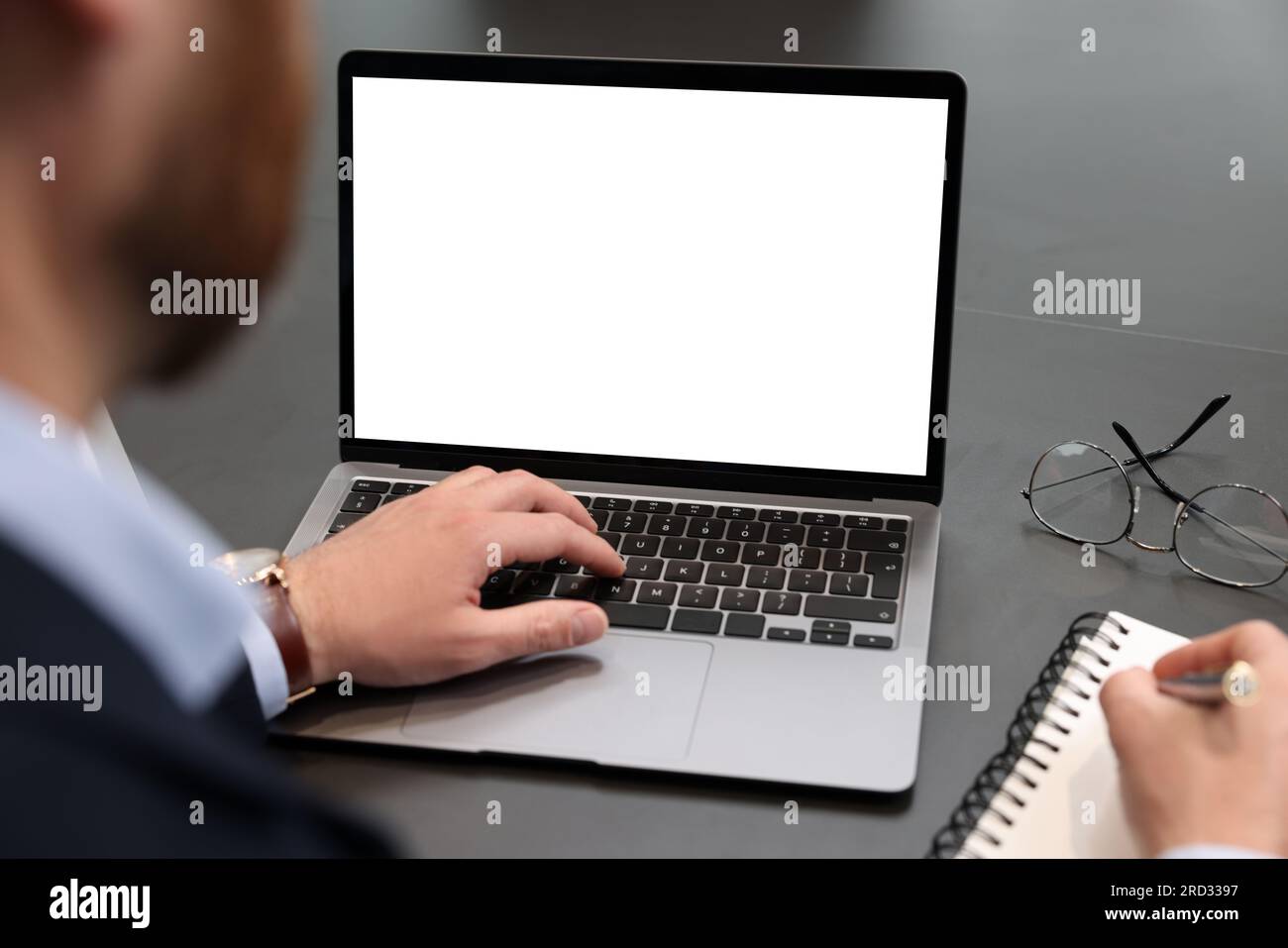 Man writing notes while working on laptop at black desk in office ...