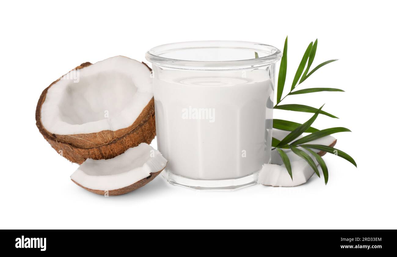 Glass of delicious vegan milk, coconut pieces and green leaves on white ...