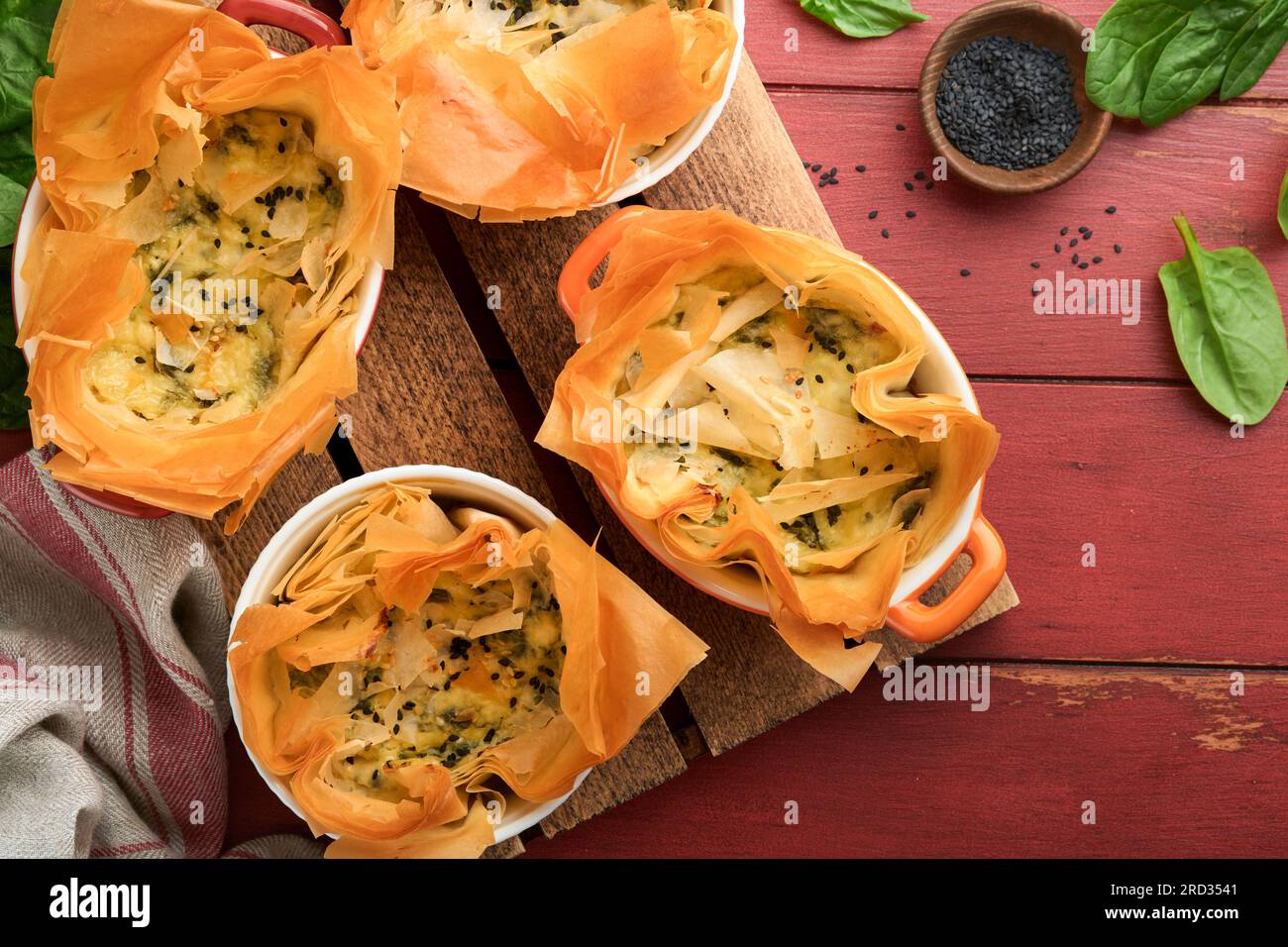 Filo pies with soft feta cheese and spinach in ceramic molds on old red ...