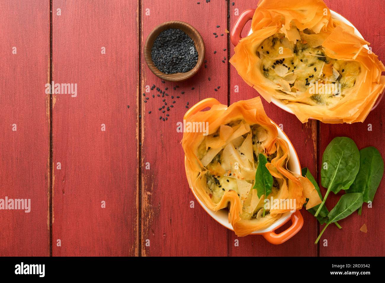 Filo pies with soft feta cheese and spinach in ceramic molds on old red ...