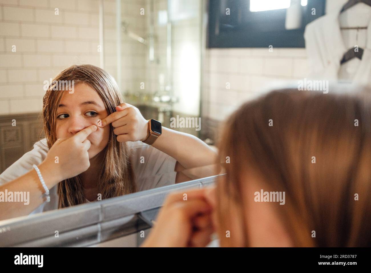 Cute teenage girl squeezes out a pimple on her cheek in the bathroom. A ...