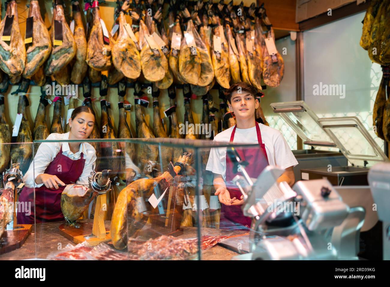 Young female and male vendors arranging jamon at counter in butcher ...