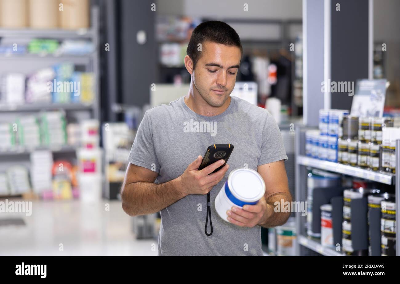 Man scanning barcode on paint can with smartphone in hardware store ...