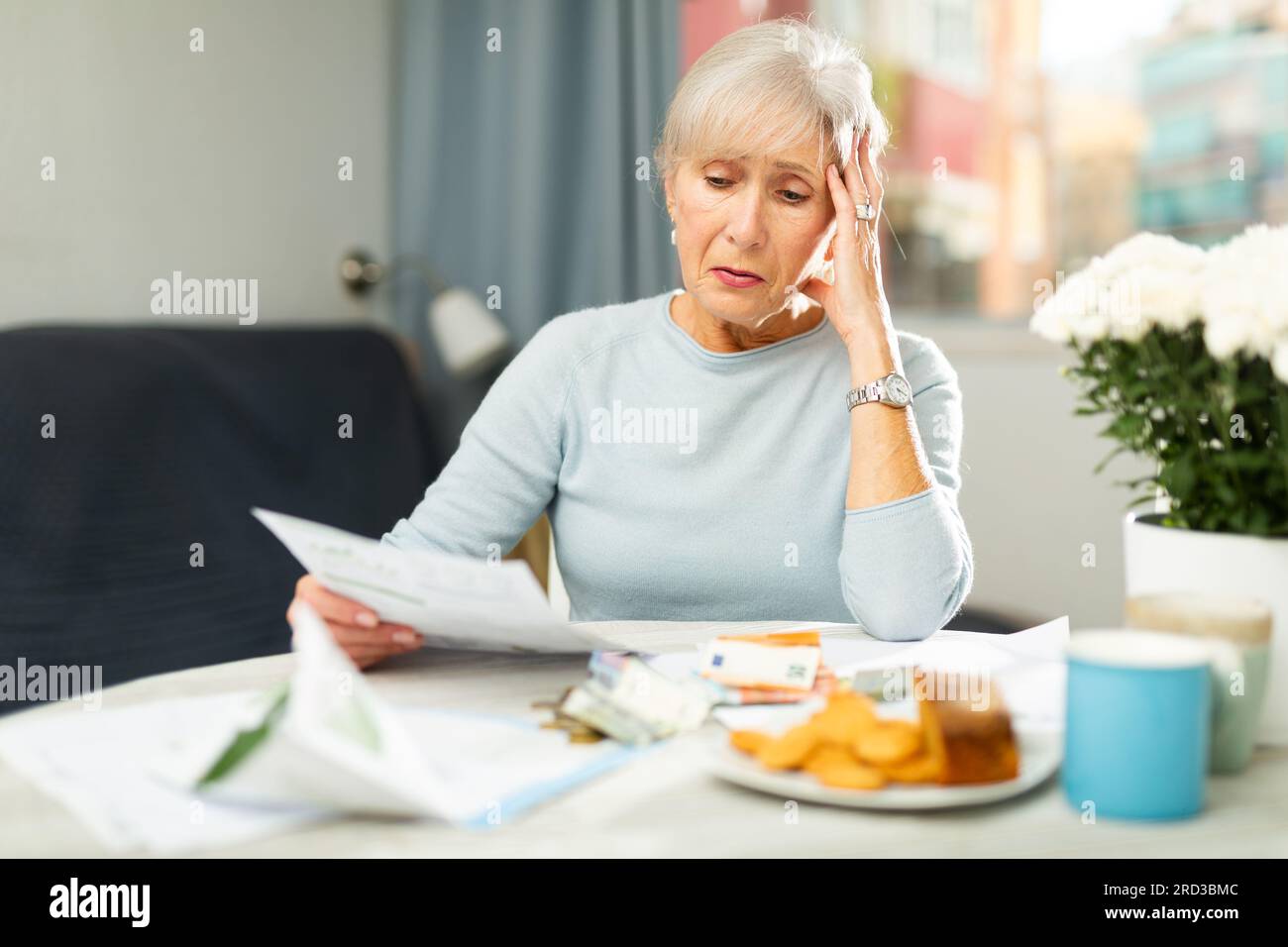 Upset senior woman looking worriedly at papers at home table Stock ...
