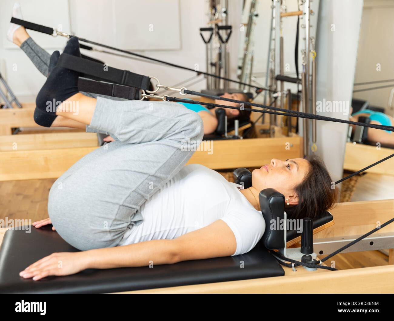 Sportswoman stretching body on pilates chair while doing forward bends ...