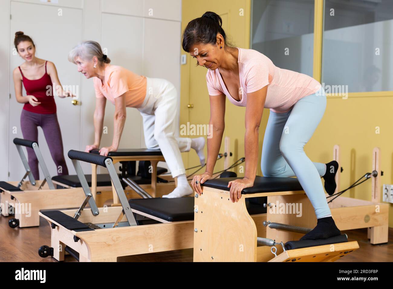 Female instructor helps women perform an exercise on a combined chair ...