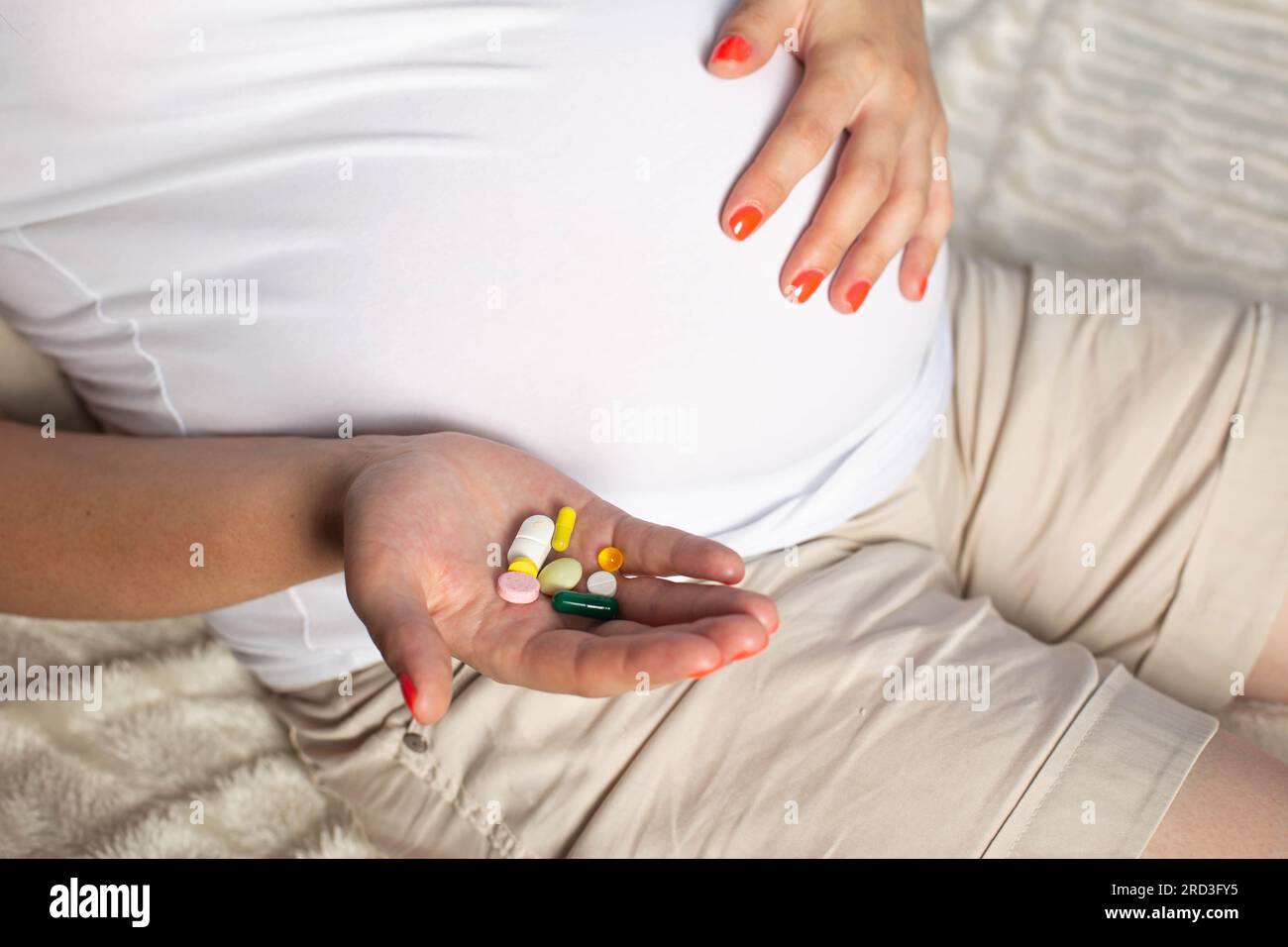 A pregnant girl holds a handful of pills in her palm against the ...