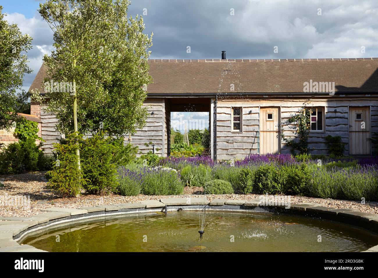 Courtyard with wood clad buildings, gravel path, pond and planting ...