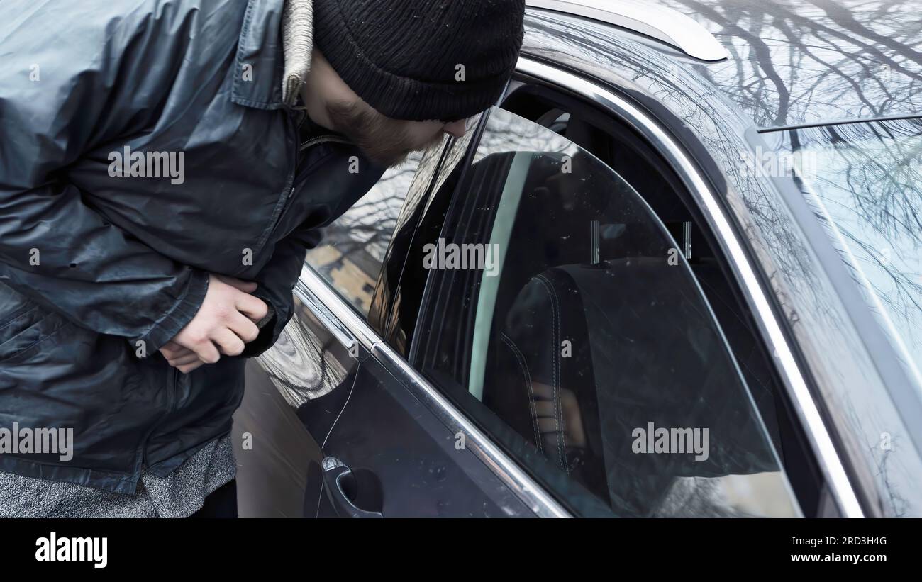 Male burglar robber passing by lookes through crack in window of parked ...