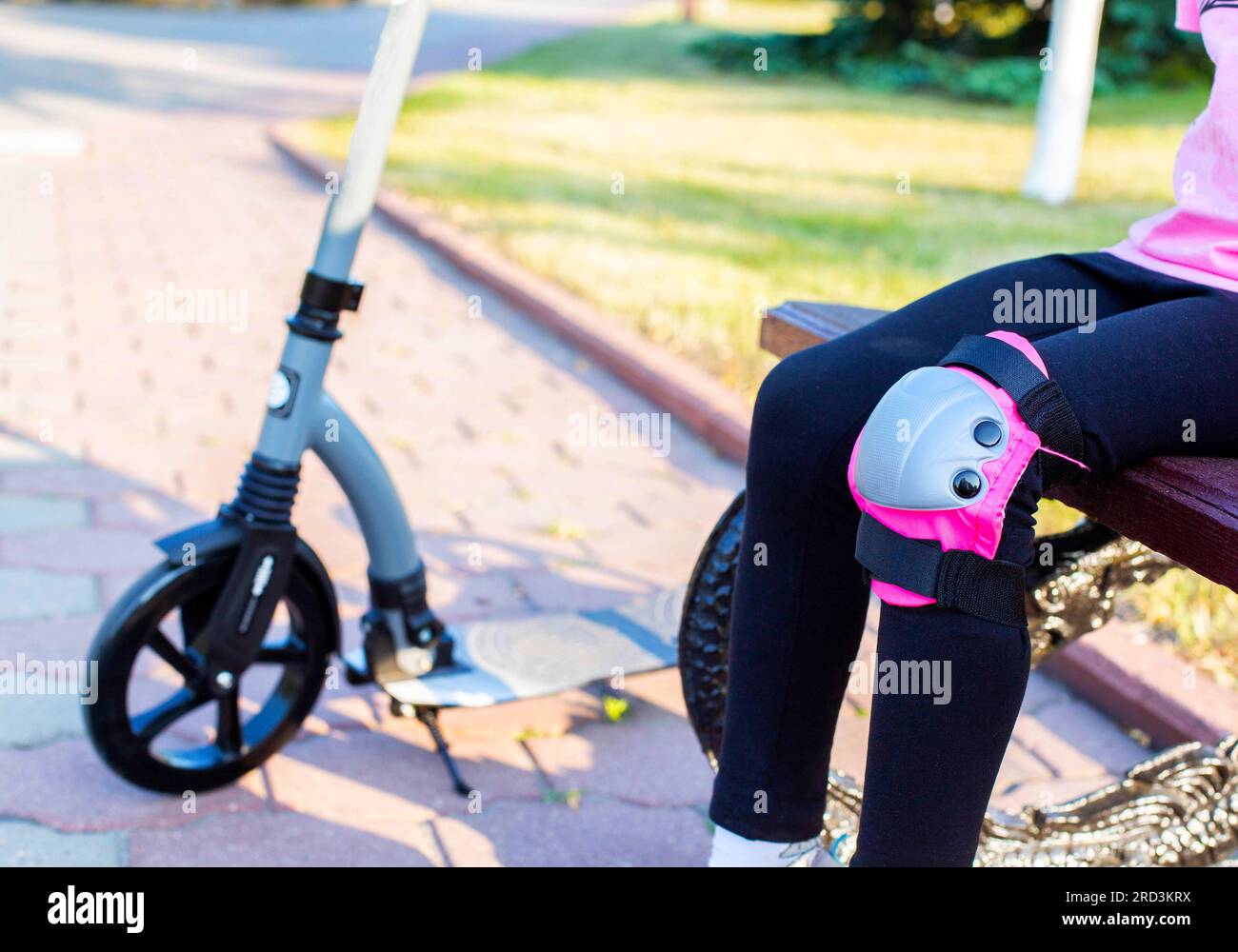 The girl is sitting on a bench in knee pads while riding a scooter ...