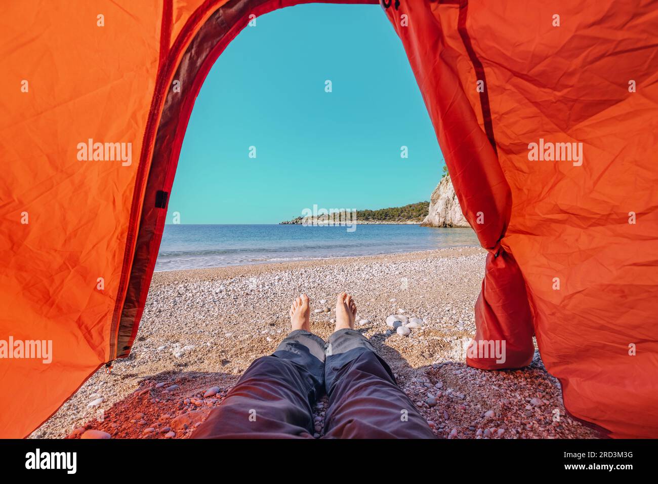a hiker's barefoot legs inside a camping tent set up on a wild sandy ...