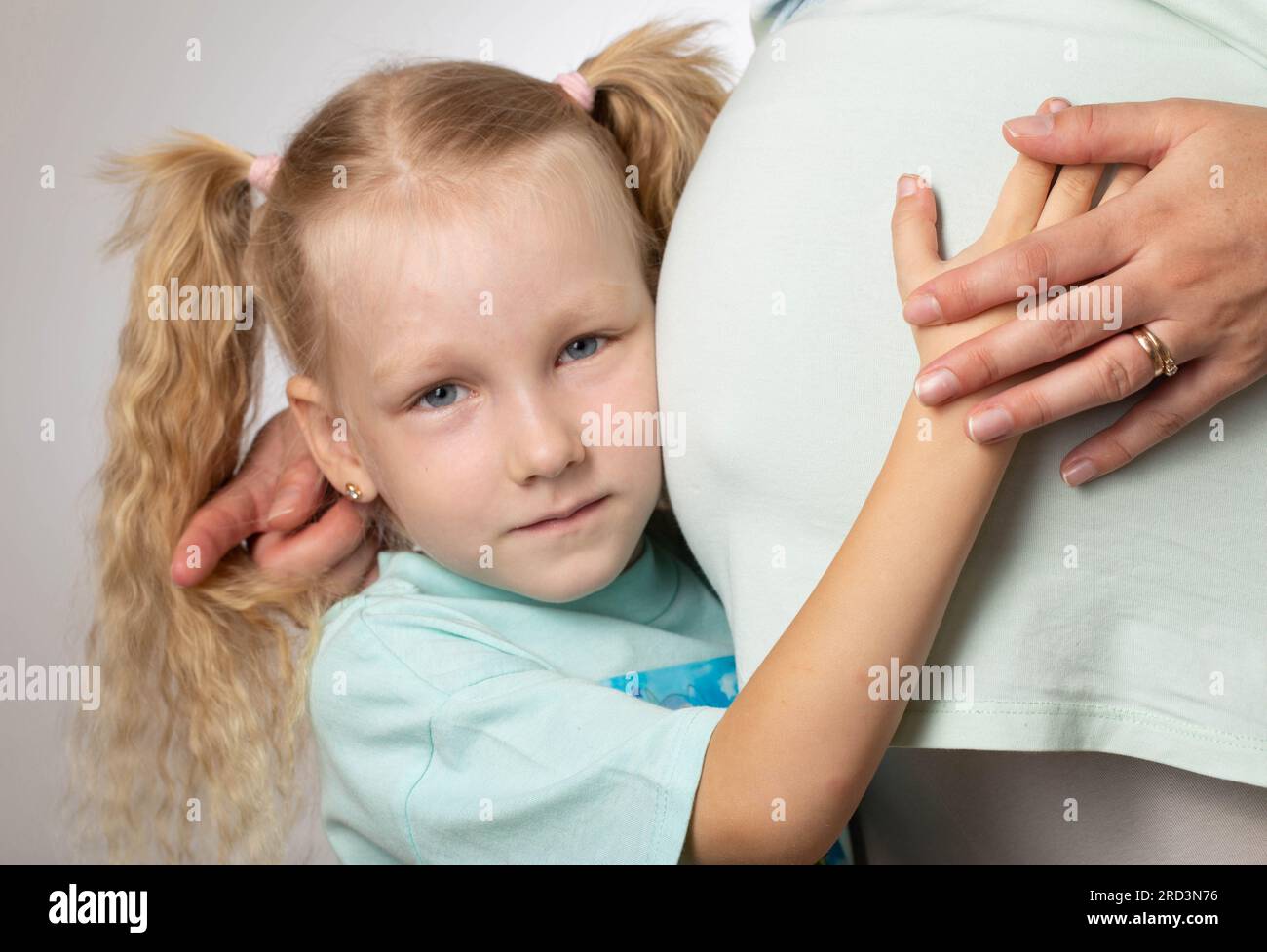 A beautiful smiling girl hugs her pregnant mother's big belly. In ...