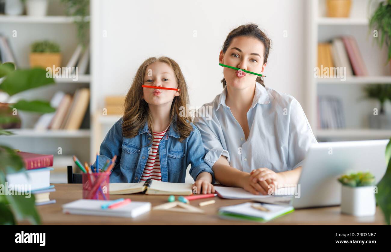 Happy child and adult are sitting at desk. Girl doing homework or ...