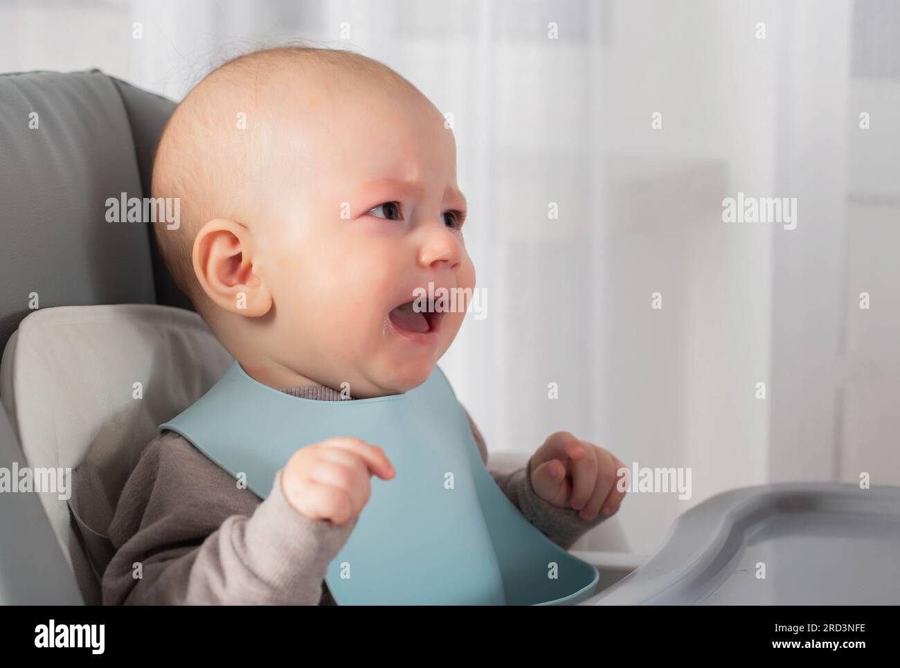 A crying baby in a bib before eating. Refusal of food in babies, poor ...