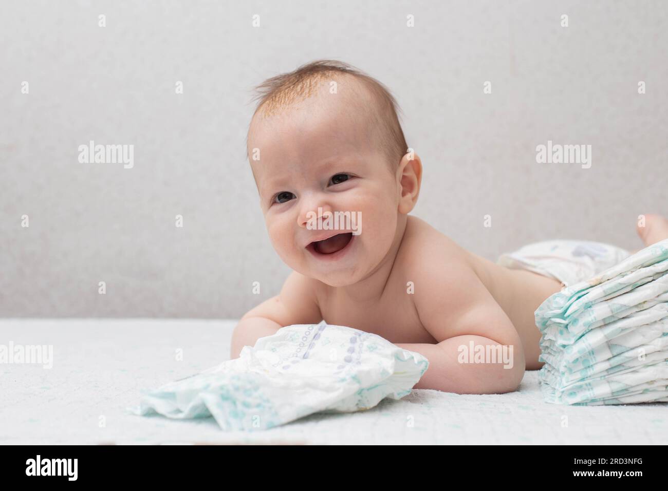 A little boy at the age of 5 months lies in a diaper on a white ...