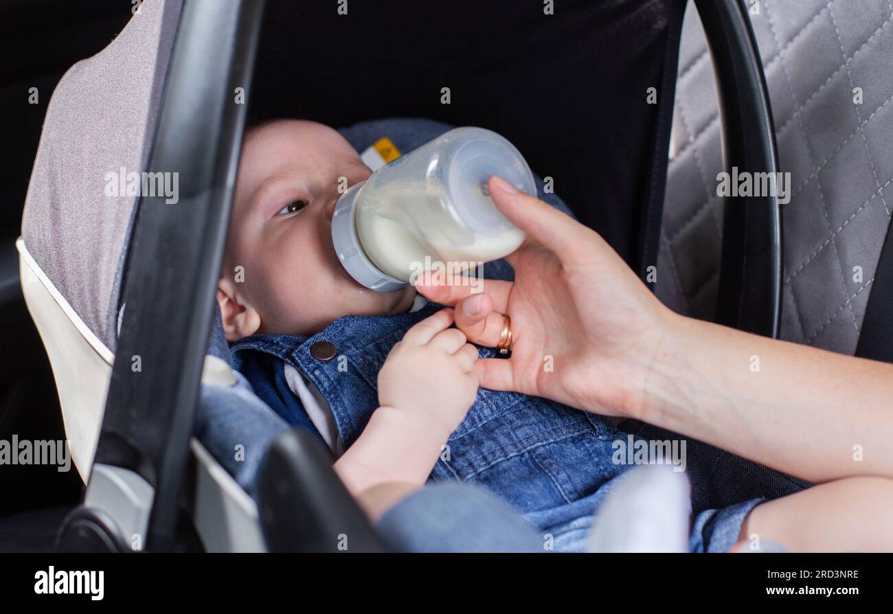 A mother feeds her baby son with milk in a car in a car seat. Safety in ...