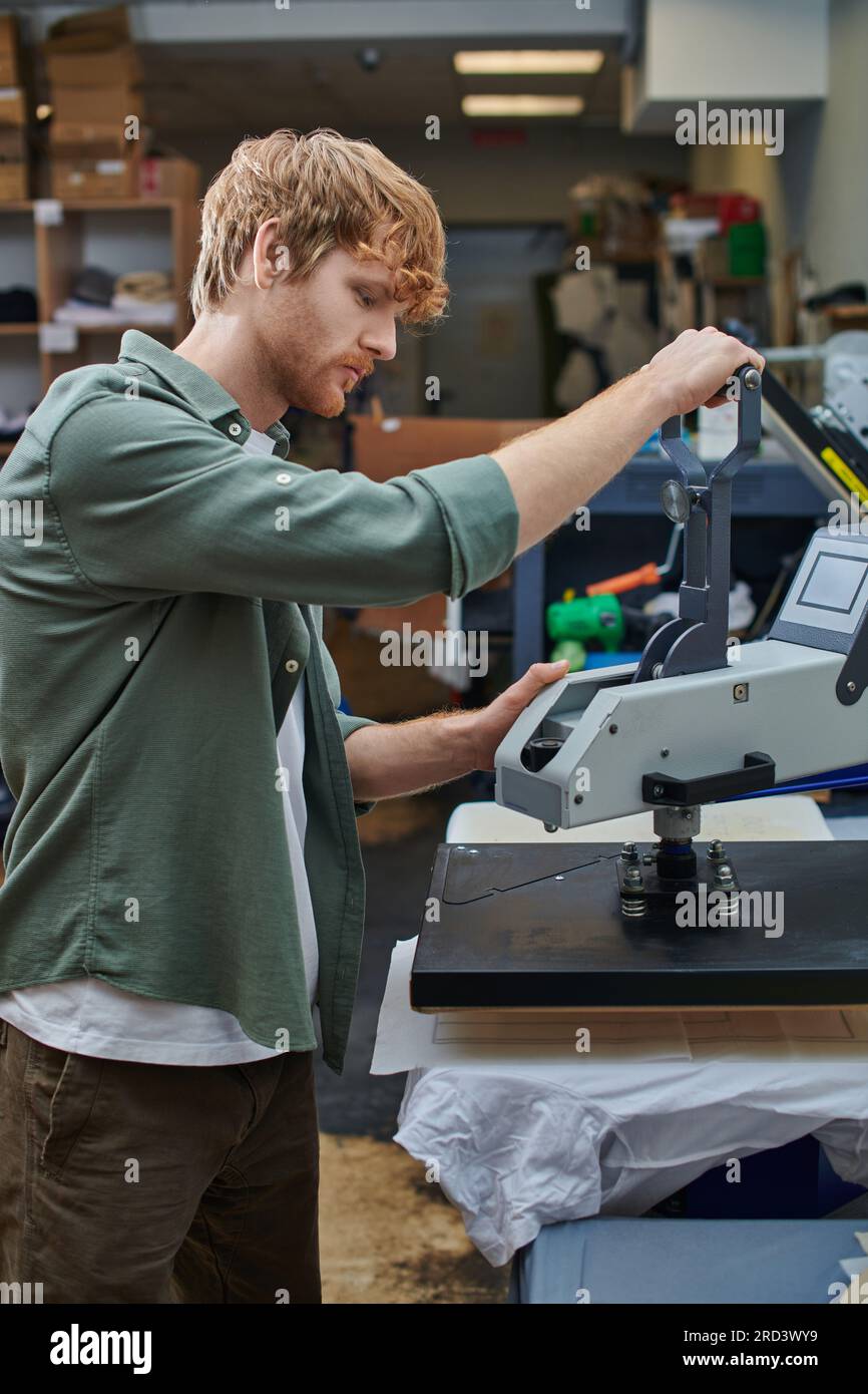 Side view of young redhead craftsman working with screen printing ...