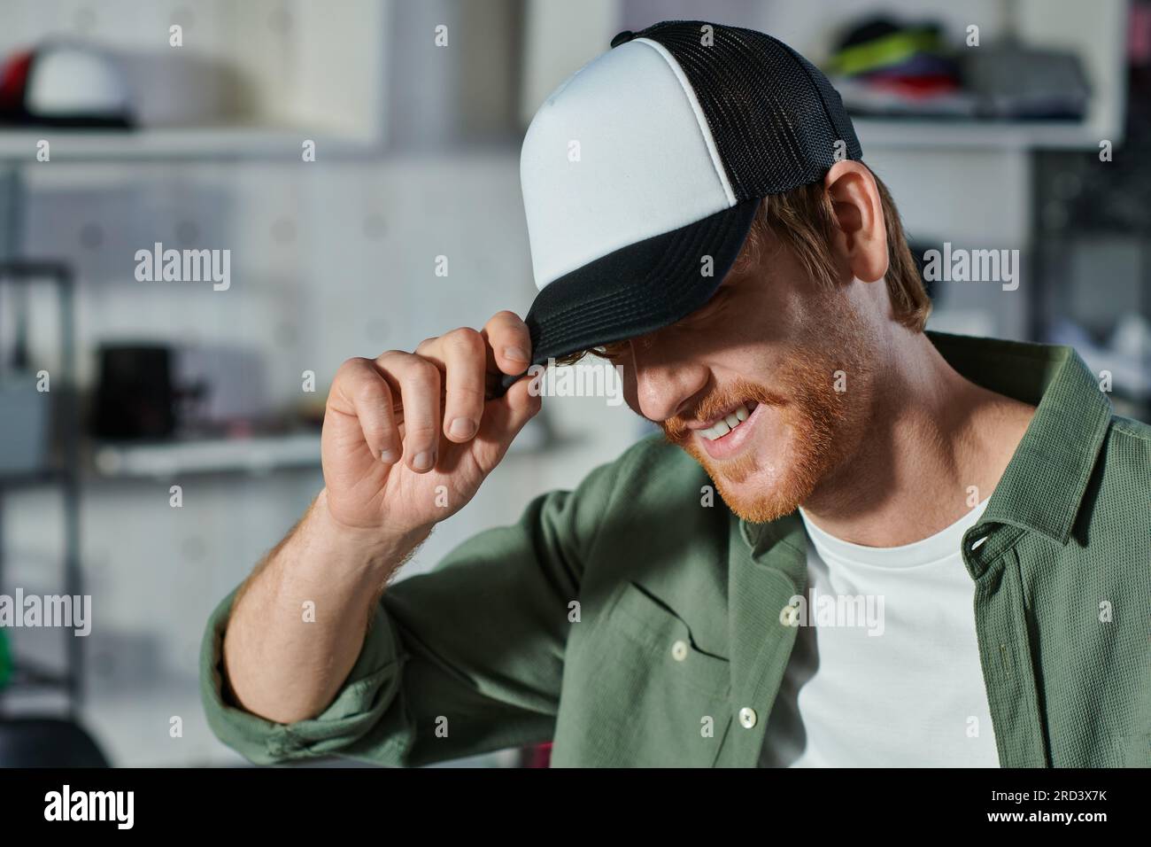 Smiling young redhead craftsman wearing snapback while working and ...