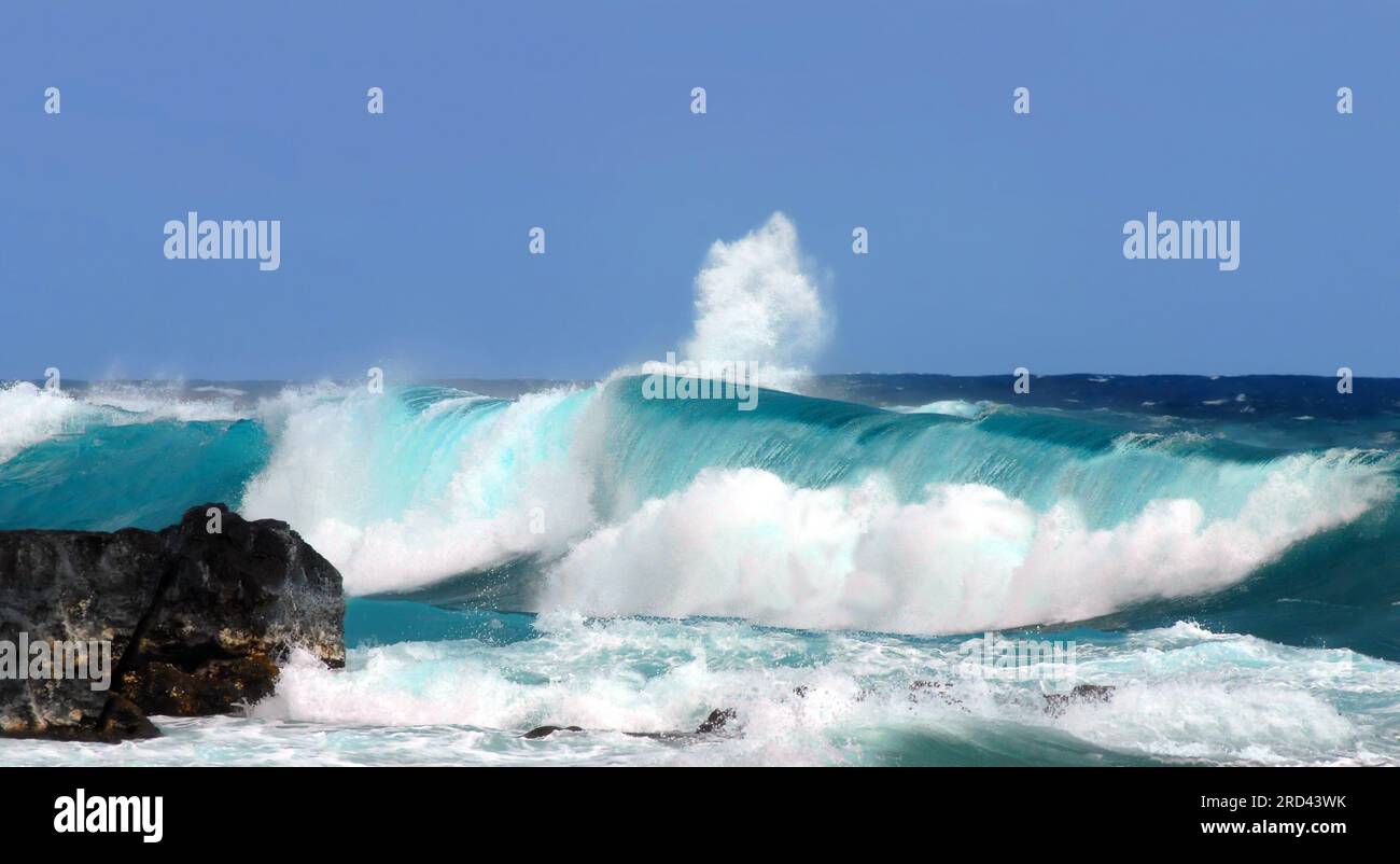 Black lava rocks form a rocky beach with aqua blue water. Waves are ...