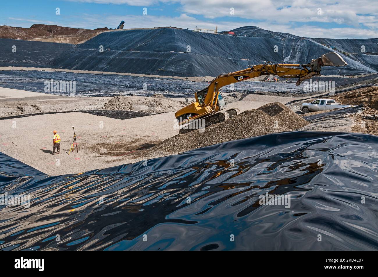 Workers and a power shovel work to excavate and install geomembrane in ...