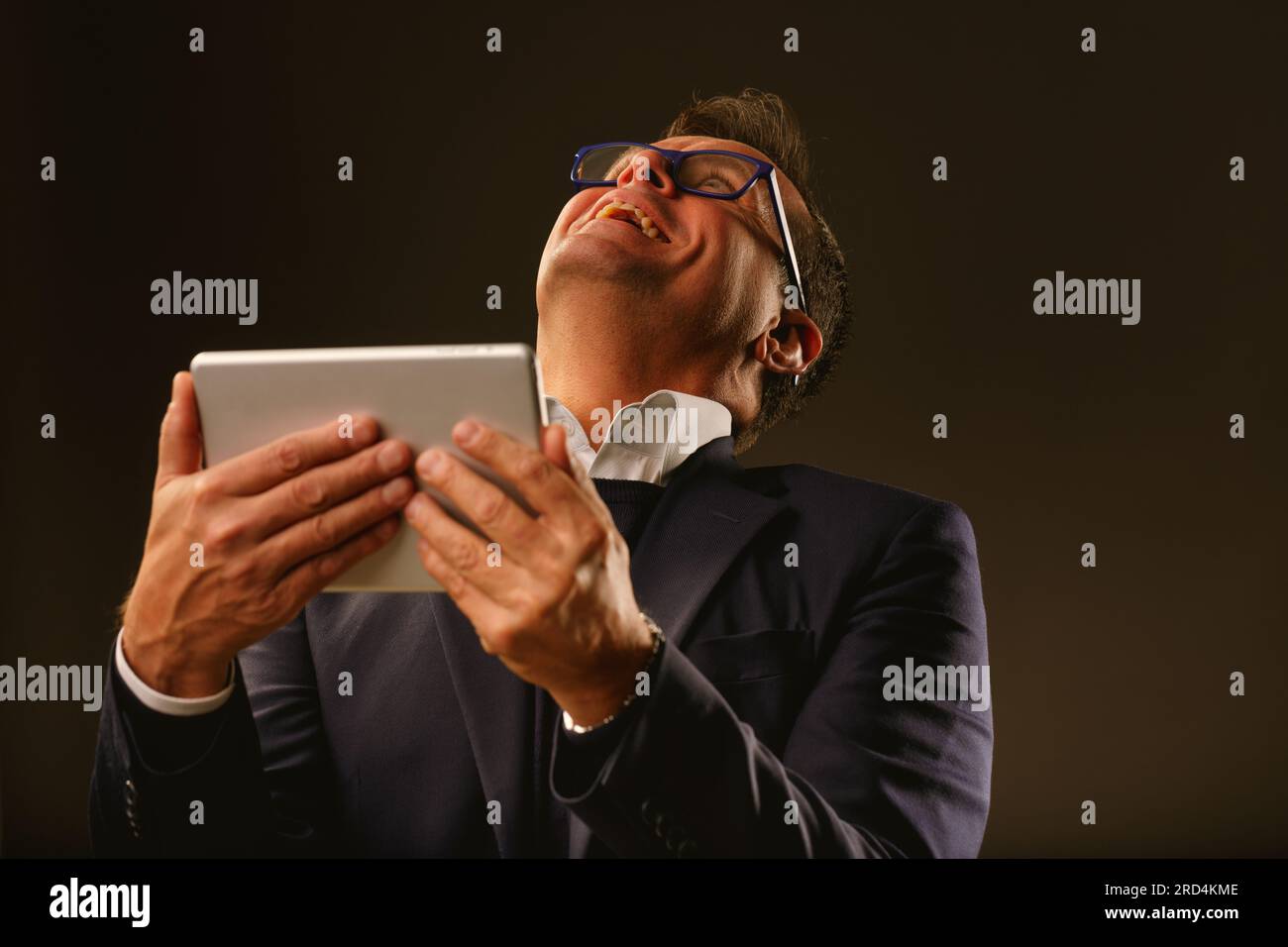Man with digital tablet laughs heartily, head thrown back in mirth ...