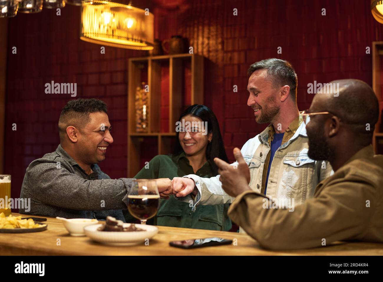 Two young cheerful men giving each other punch bump while standing by ...