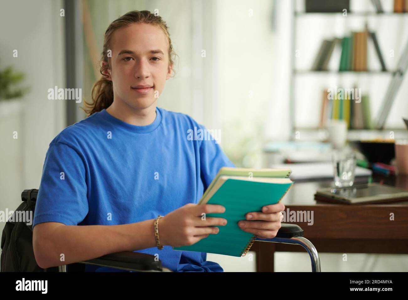 Portrait of high school student with disability studying in library ...