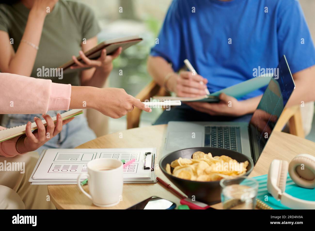 Hands of teenagers eating snacks while discussing website wireframe ...