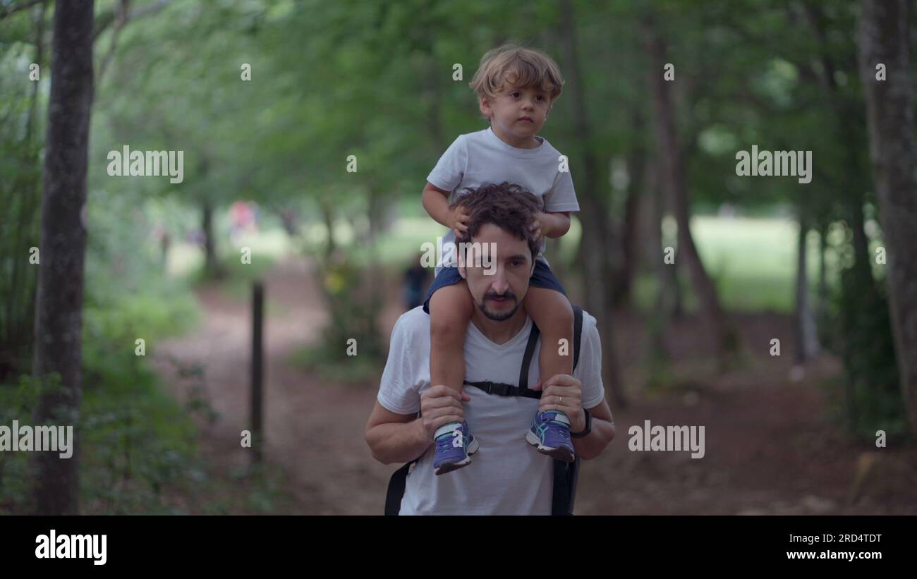 Parent and kid hiking together in the woods child on father shoulders ...