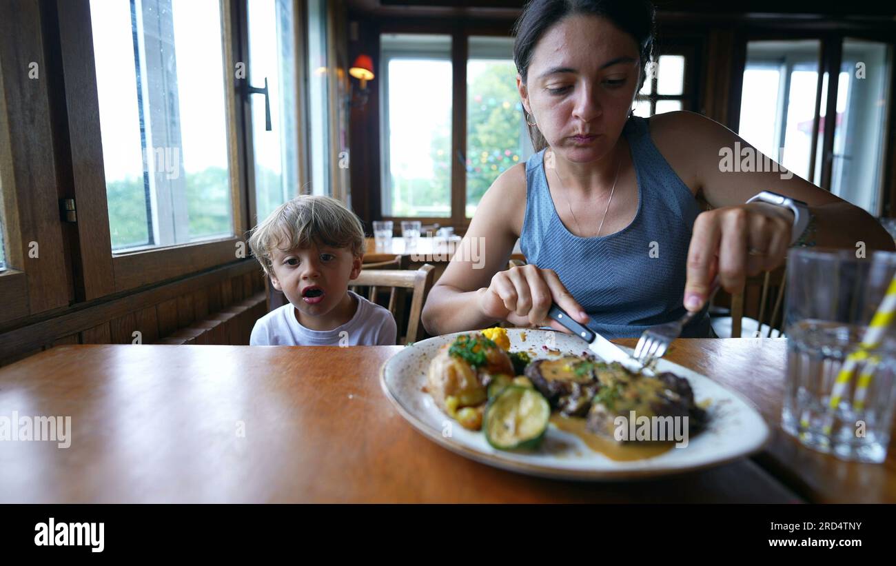 Parent and child at restaurant mother cutting meat eating food Stock ...