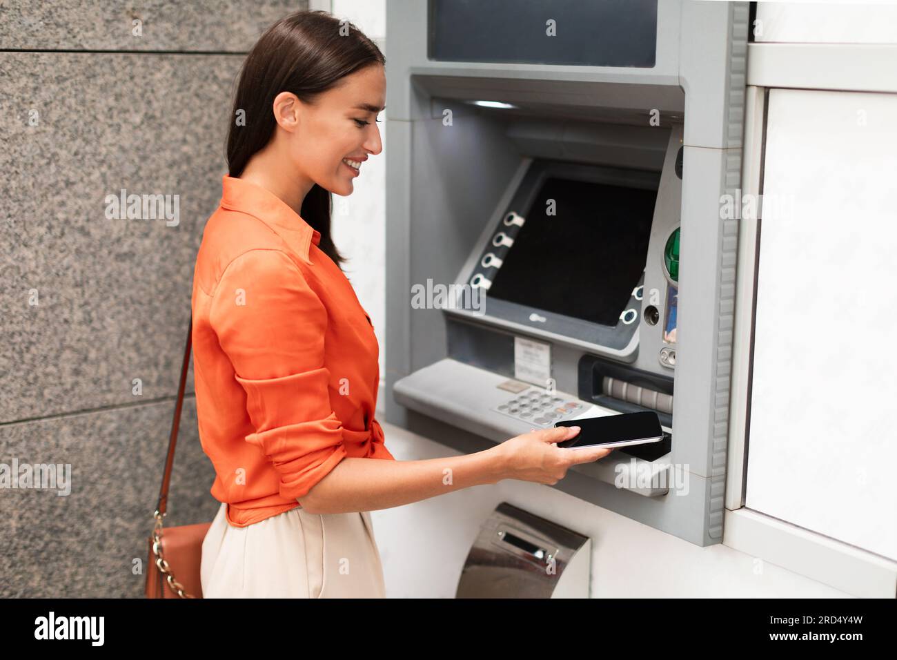Lady using smartphone gaining access to ATM withdrawing money outside Stock Photo - Alamy