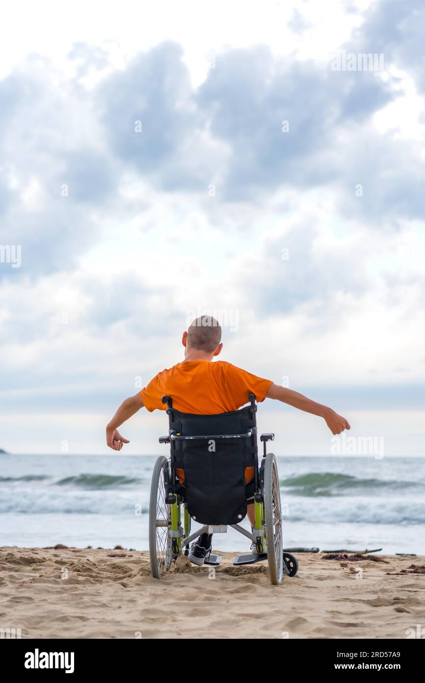 A disabled person on his back in a wheelchair on the beach in summer by ...