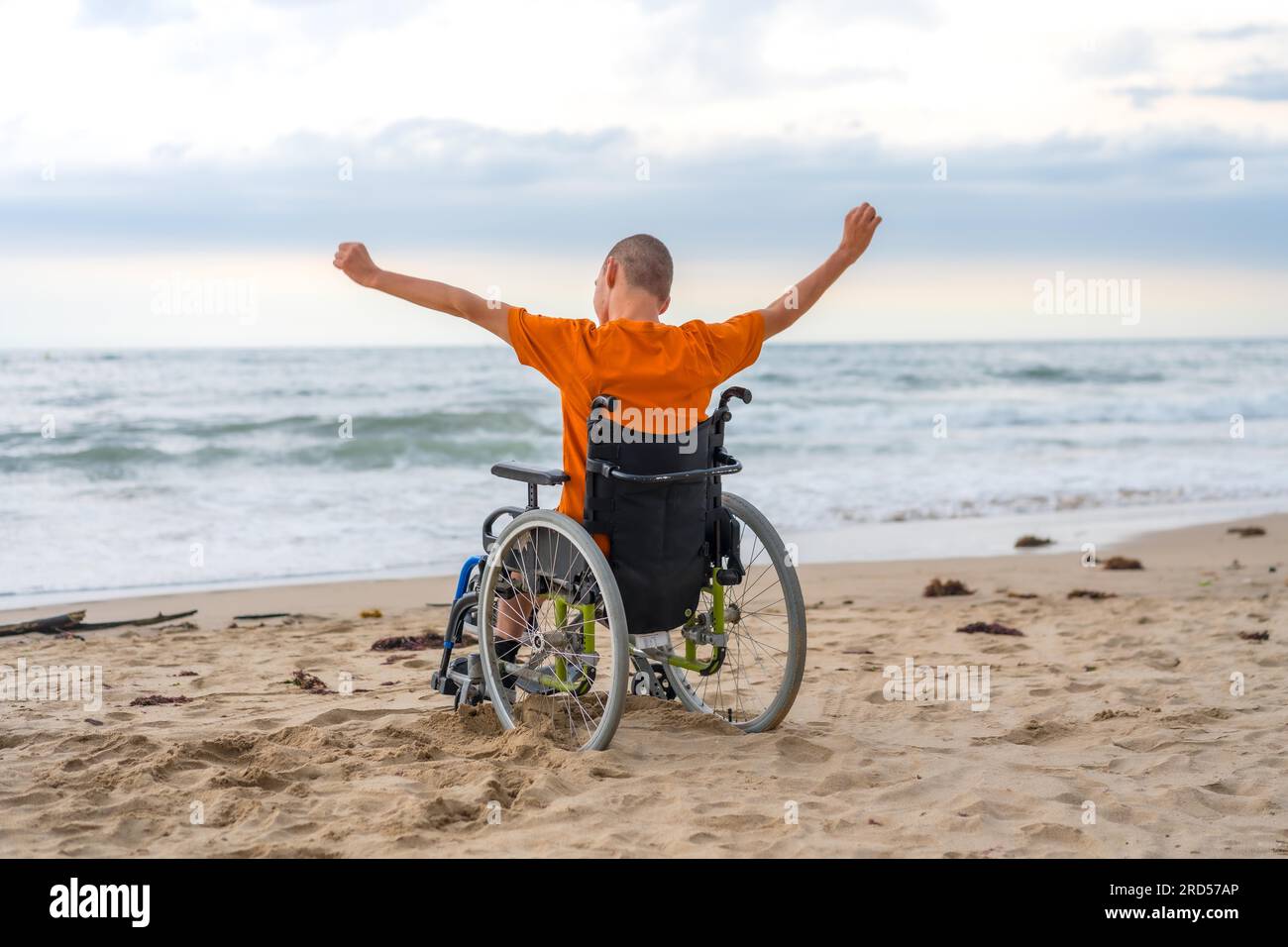 Disabled person on his back in a wheelchair on the beach with open arms ...