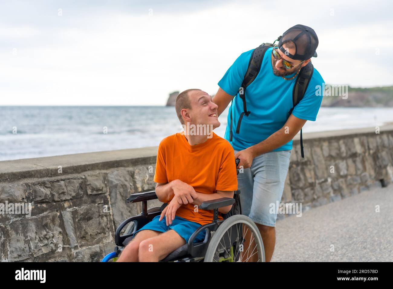 Disabled person in a wheelchair being pushed by a friend on the beach ...