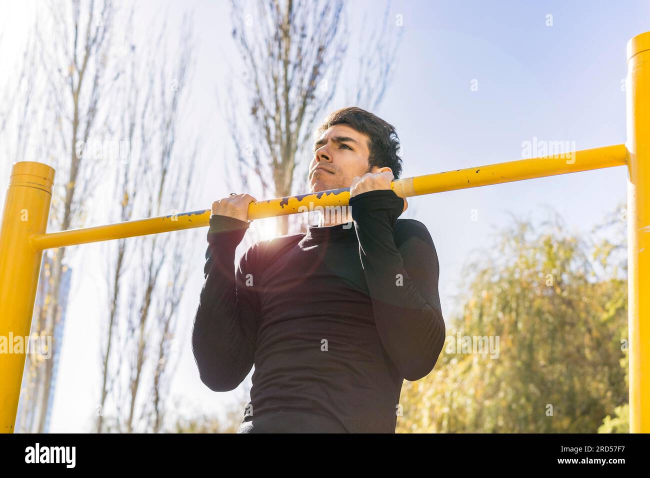 Attractive man doing pull-ups exercises on a crossbar in a public park ...