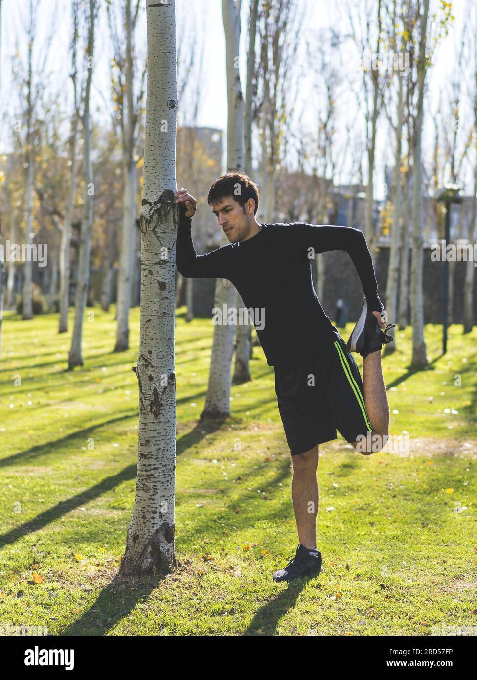 Attractive man leaning against a tree stretching his quadriceps Stock ...