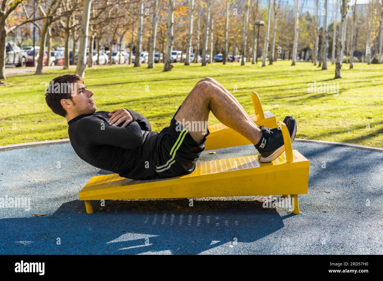 Attractive young man doing abdominal exercises on a public equipment in ...