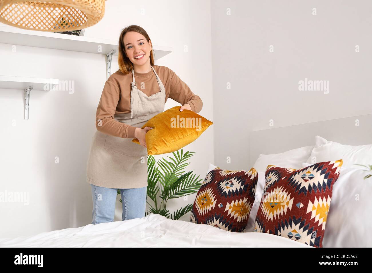 Young woman making bed in bedroom Stock Photo - Alamy