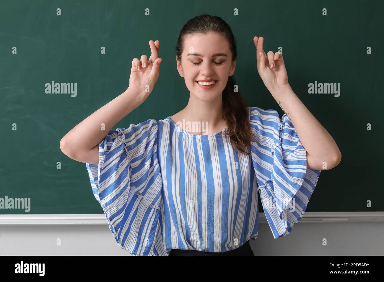 Female teacher crossing fingers near chalkboard in classroom Stock ...