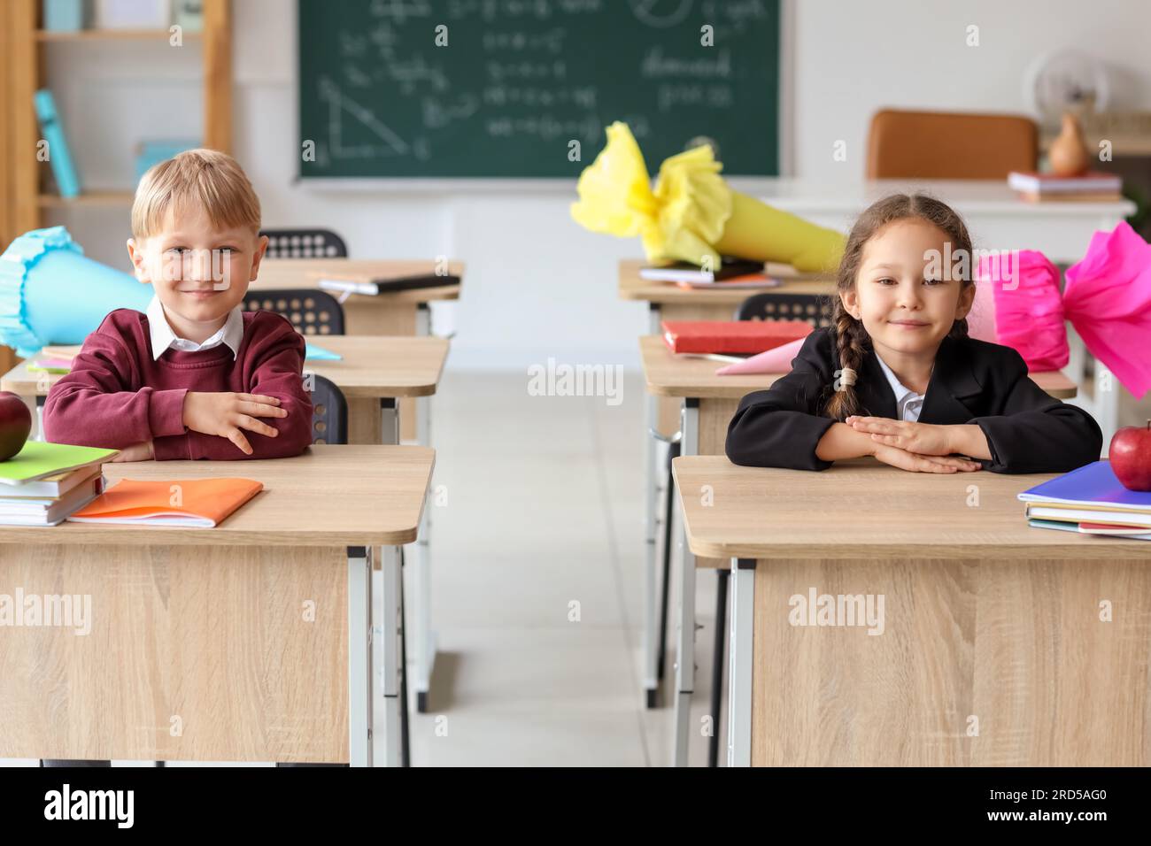 Happy classmates with school cones sitting at desks in classroom Stock ...