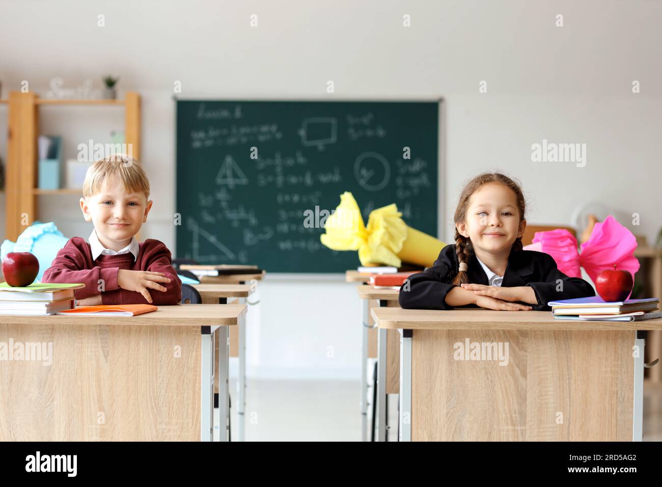 Happy classmates with school cones sitting at desks in classroom Stock ...