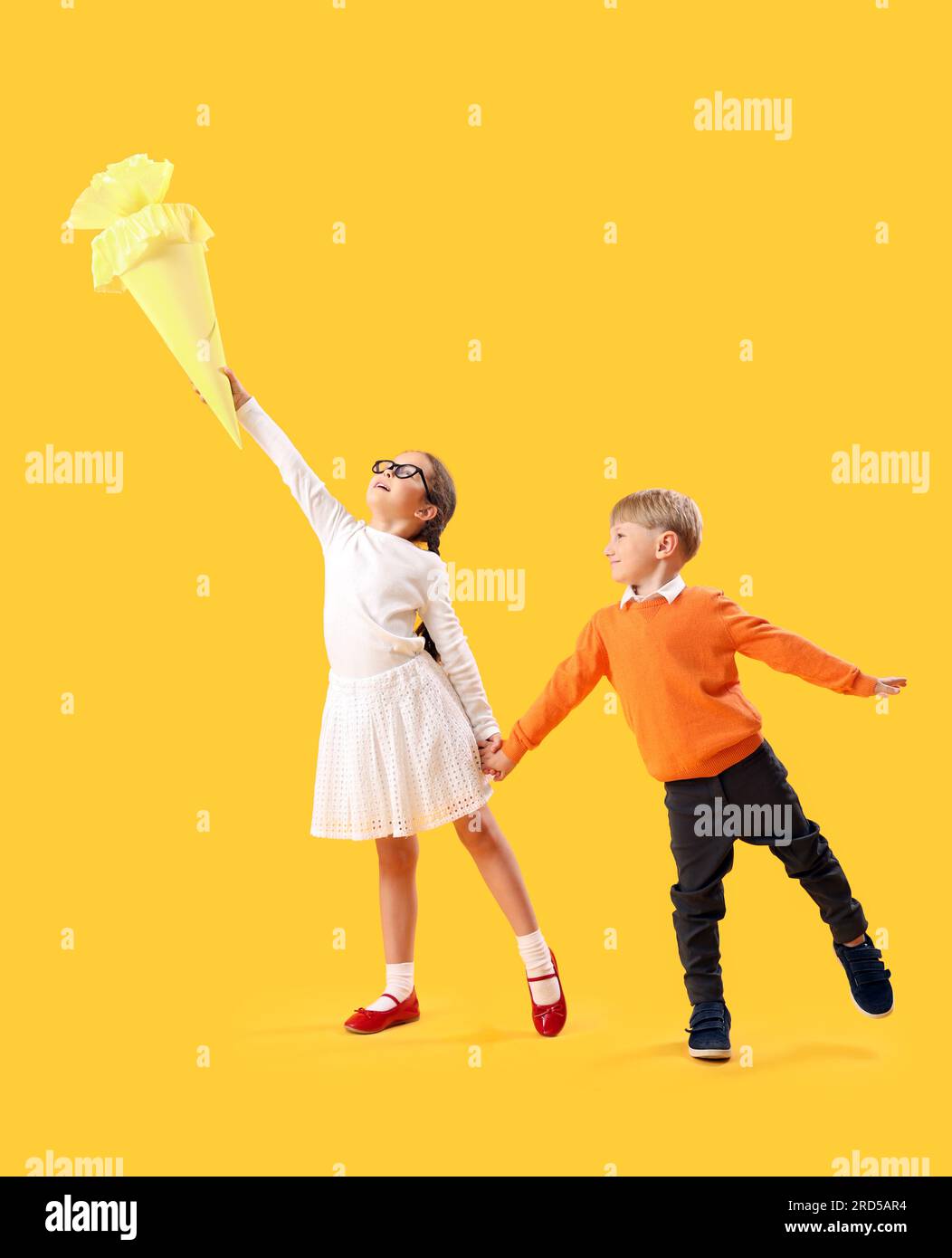 Happy little girl and boy with school cone jumping on yellow background ...