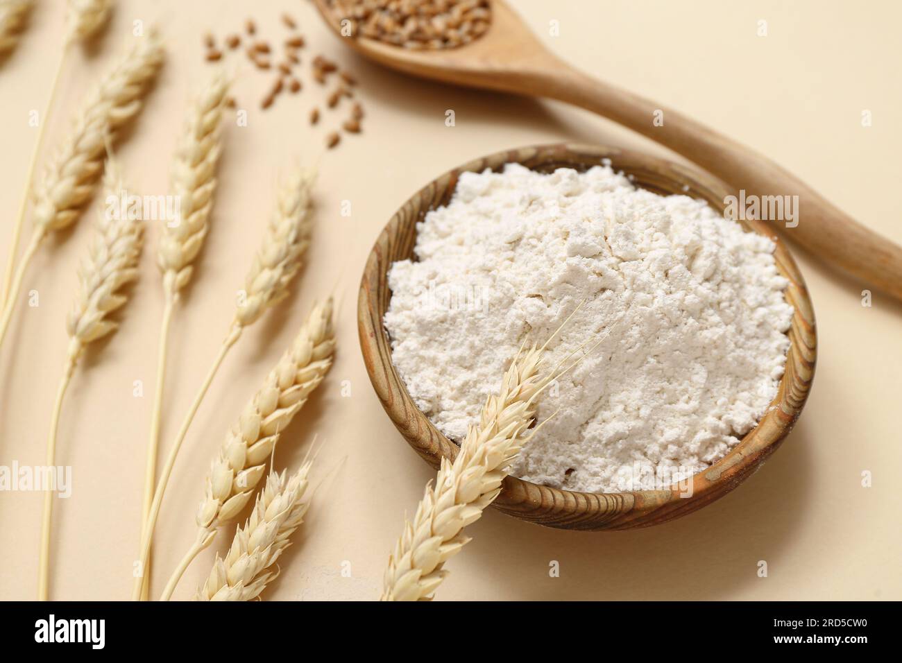 Bowl with wheat flour and spikelets on beige background, closeup Stock ...
